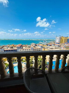 Uma varanda com vista para uma área de resort costeira, incluindo uma piscina e diversos edifícios.