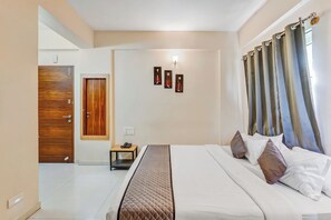Quarto de hotel com uma cama, uma mesa de cabeceira, uma porta de madeira e um candeeiro fixado na parede.