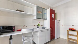 Uma cozinha com armários brancos, uma geladeira vermelha, uma torradeira e uma pequena mesa com frutas.