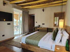 Quarto de hotel com cama, escrivaninha, televisão e janela com cortinas.