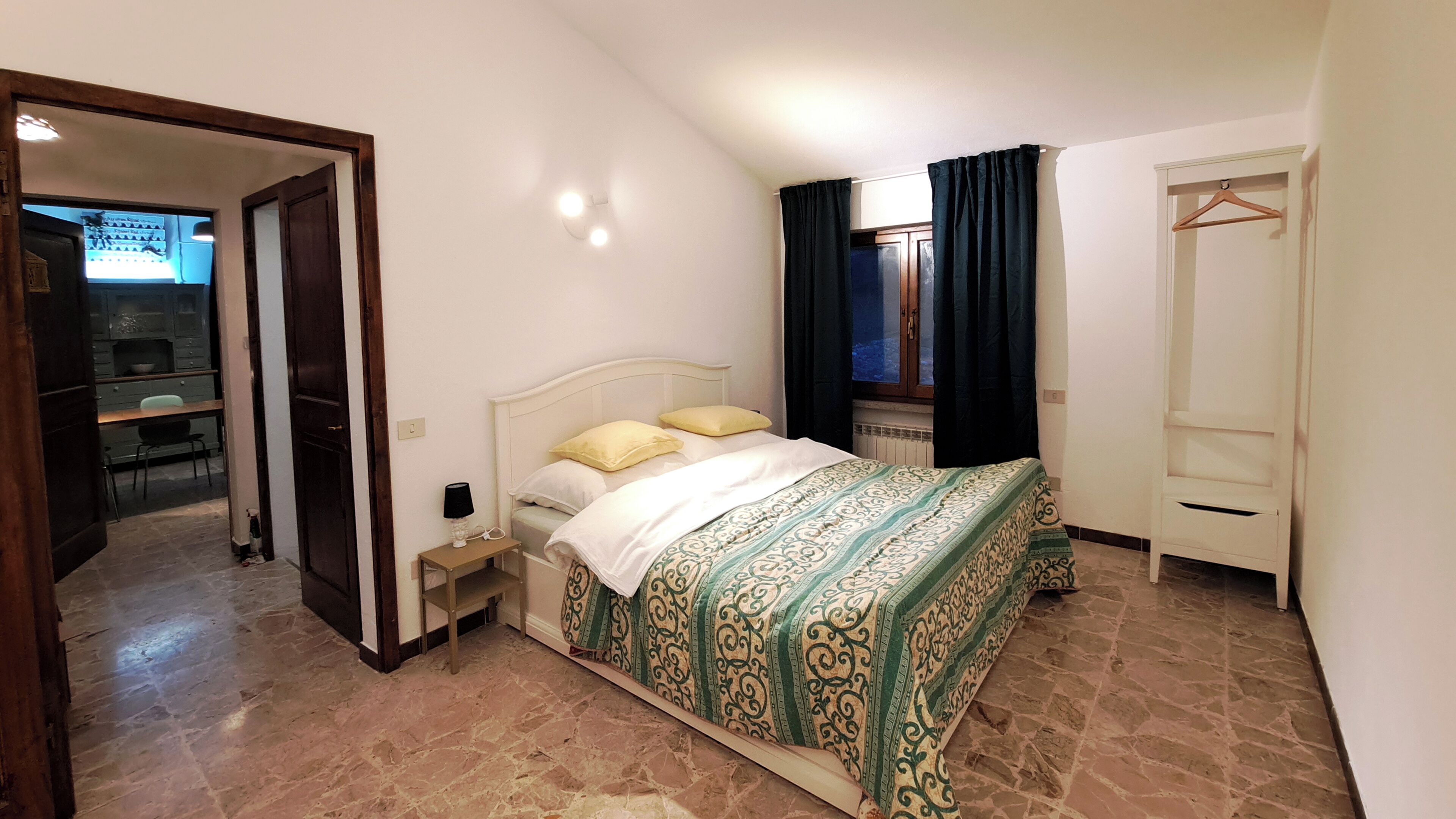 Quarto com cama, mesa de cabeceira, abajur e guarda-roupa.