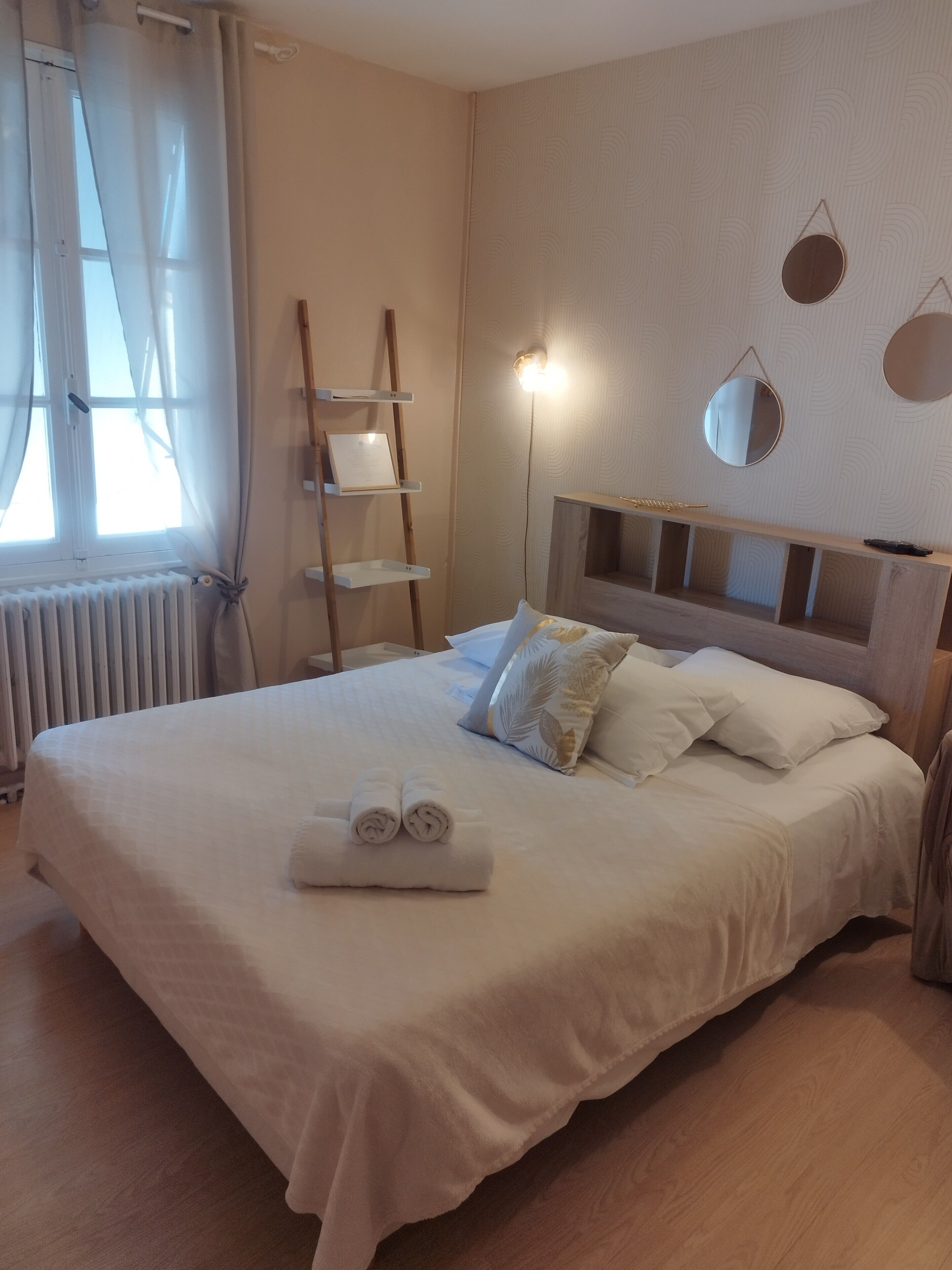 Cama bem arrumada com lençóis e almofadas brancas, uma escada de madeira e uma mesinha de cabeceira com abajur.