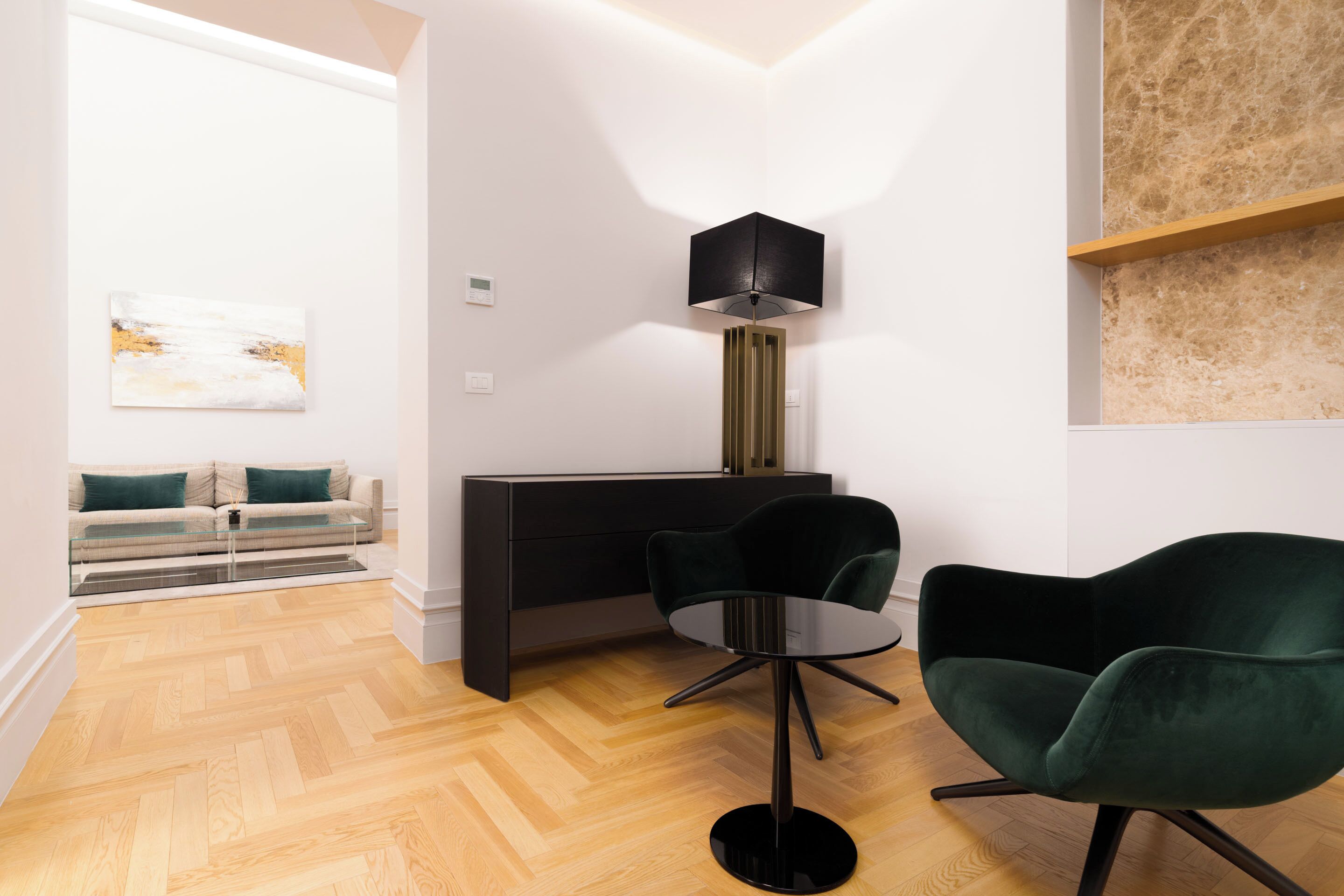 Uma sala de estar moderna com um sofá, uma mesa de centro de vidro, uma escrivaninha preta, uma poltrona verde e um abajur.