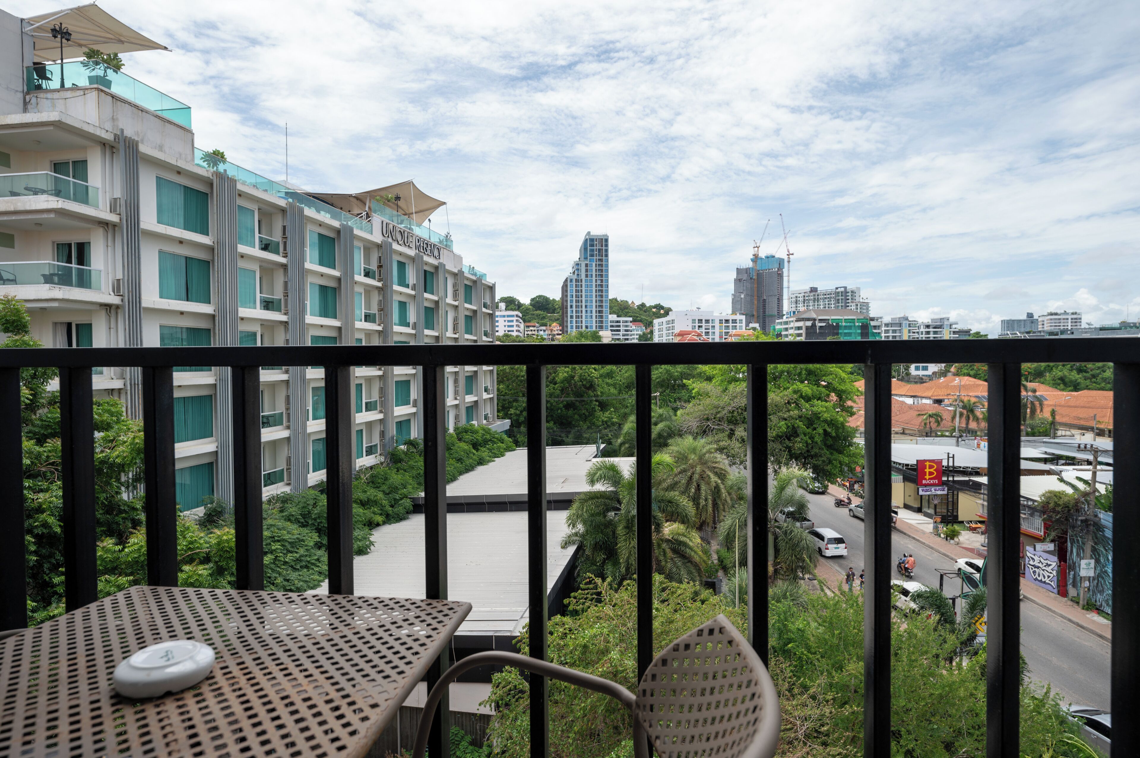 Uma varanda com mesa e cadeiras, com vista para um horizonte urbano com edifícios e uma estrada.