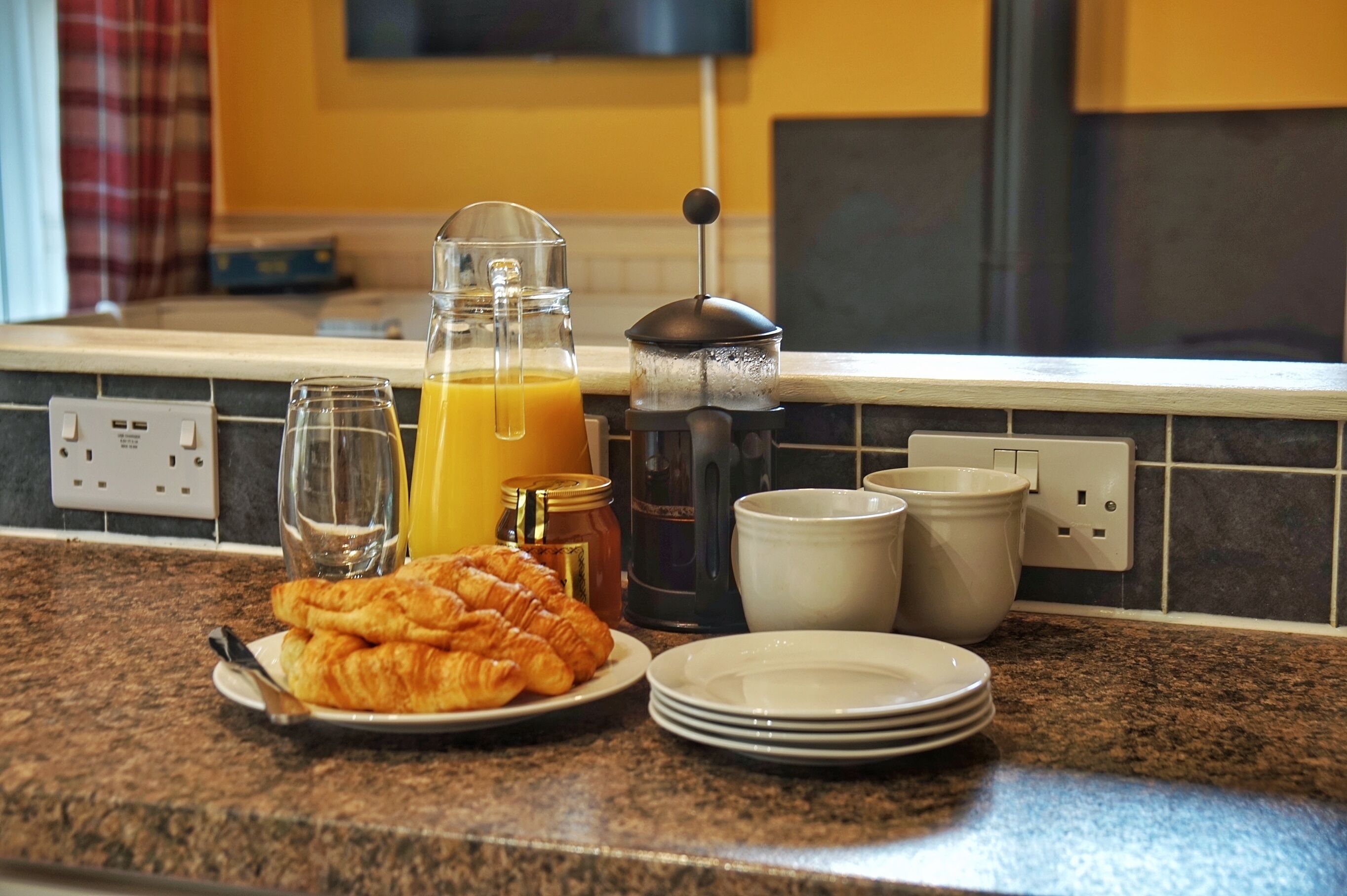 Disposição para o café da manhã com croissants, suco de laranja, café e jarras de café em uma bancada de cozinha.
