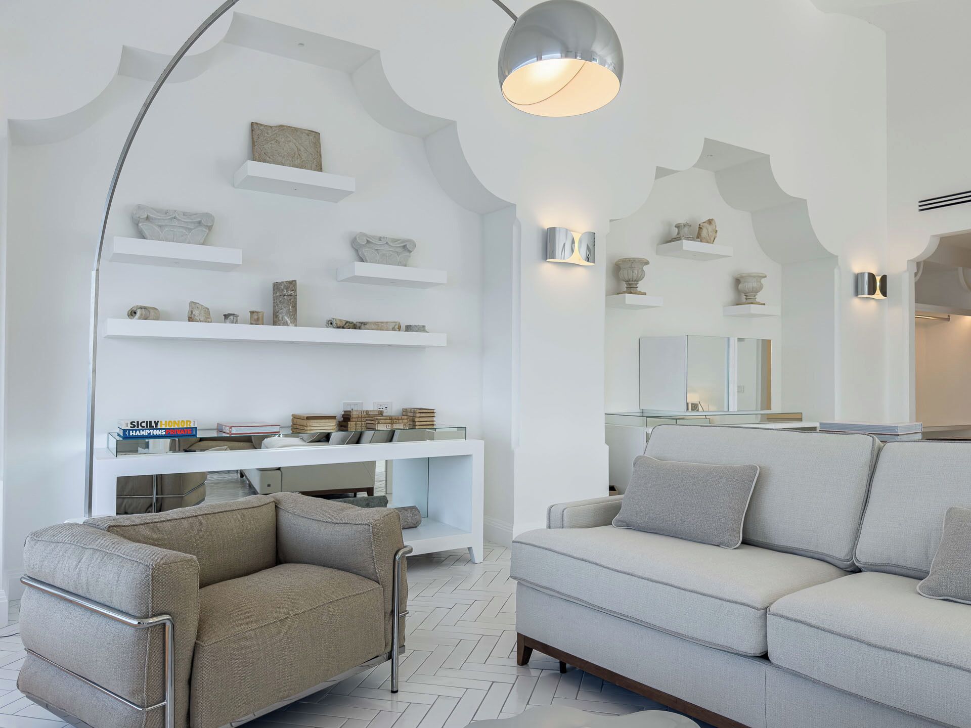 Uma sala de estar moderna com um sofá, poltronas, uma mesa de centro e uma estante com objetos decorativos.