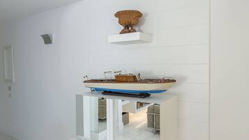 Um modelo de navio sobre um suporte branco em um corredor com paredes brancas e piso de azulejos.