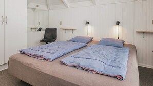Quarto com cama de solteiro, uma cadeira, escrivaninha e luminárias de parede.