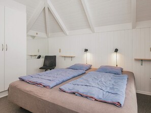 Quarto com cama de solteiro, uma cadeira, escrivaninha e luminárias de parede.