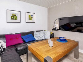 Uma sala de estar moderna com uma mesa de centro de madeira, um sofá de couro preto com almofadas coloridas e duas quadros nas paredes.
