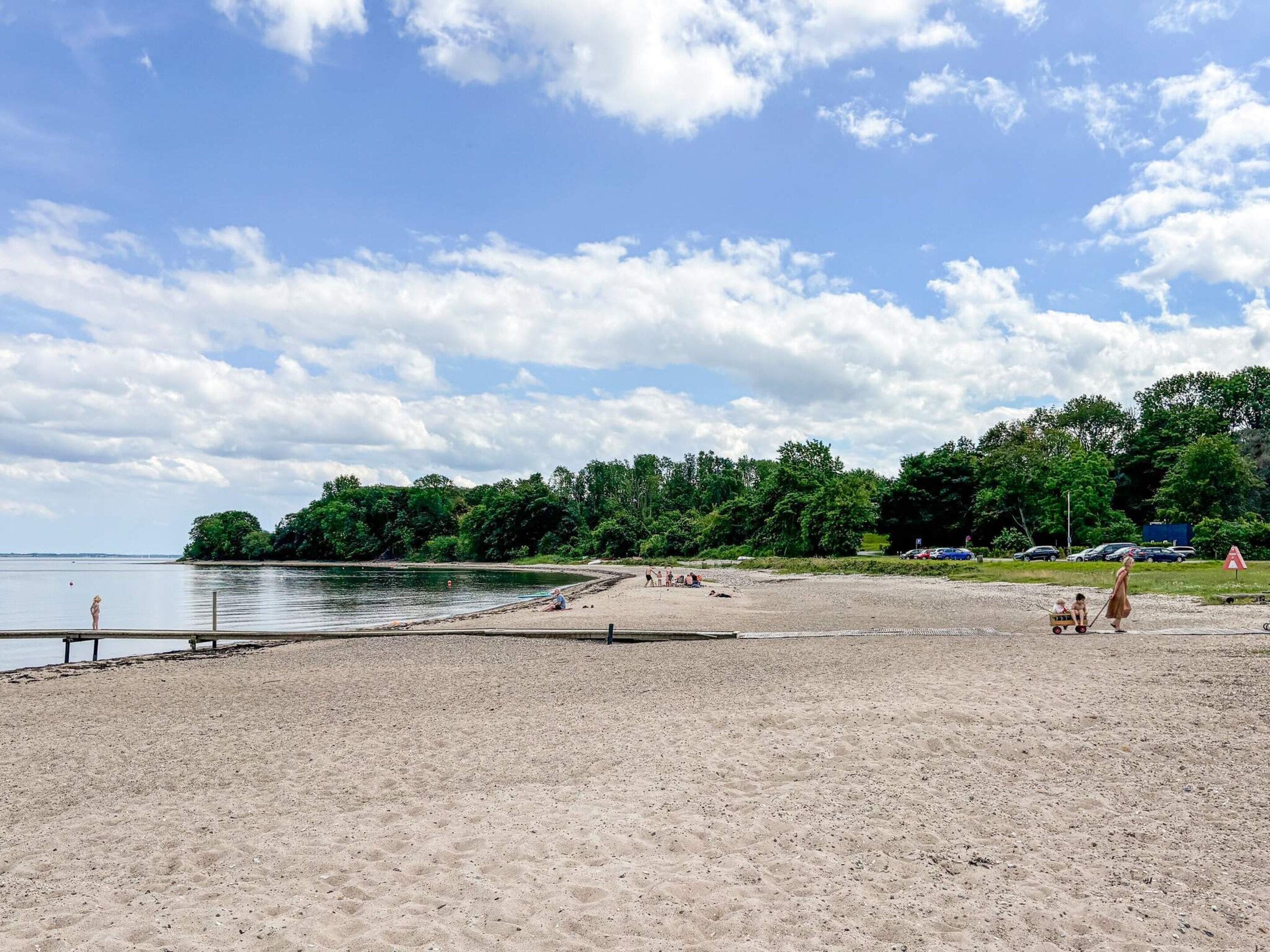 Uma praia com areal, um cais e uma área arborizada ao fundo.