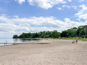 Uma praia com areal, um cais e uma área arborizada ao fundo.