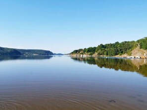 Um lago tranquilo com céu limpo, rodeado por colinas e alguns edifícios.