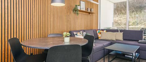 Uma sala de estar moderna com uma mesa de jantar redonda, cadeiras pretas, um sofá cinza e uma mesa de centro preta.