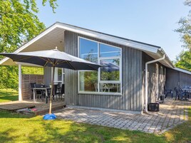 Uma casa de madeira com varanda coberta, uma janela grande e um deck com móveis de exterior.