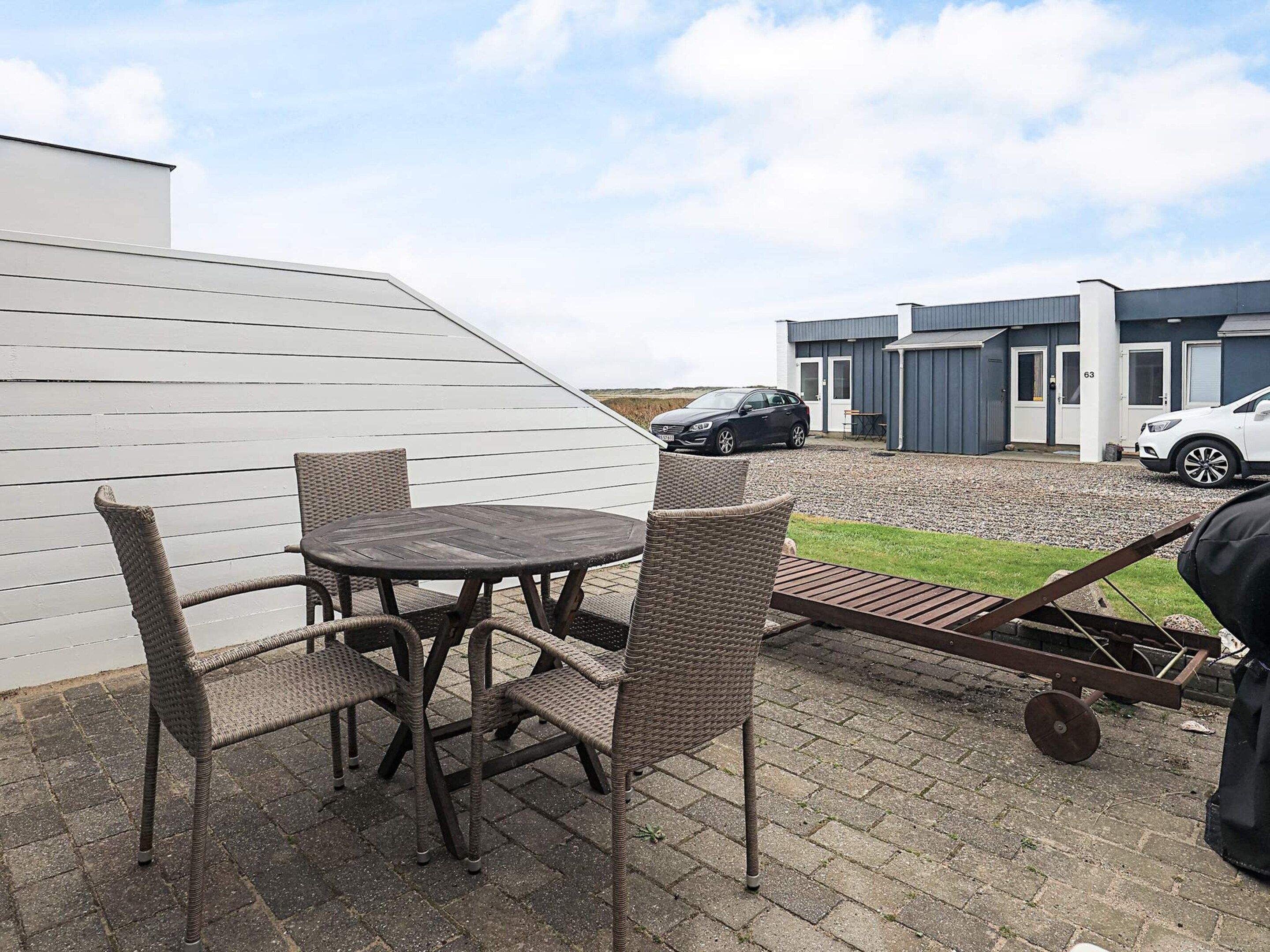Um pátio externo com móveis de vime e um carrinho para churrasco.