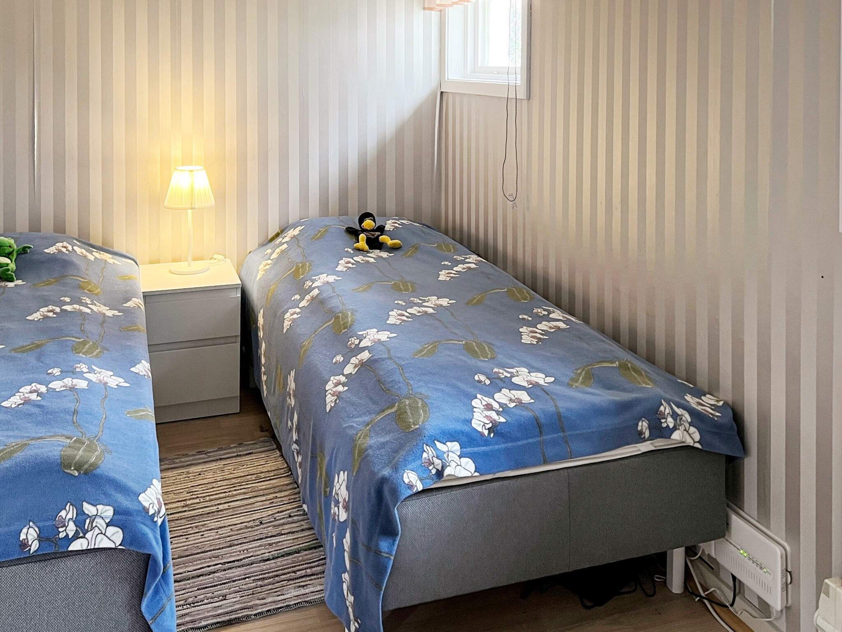 Quarto duplo com duas camas, mesa de cabeceira, luminária e janela.