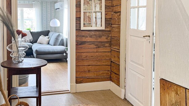 Quarto com parede de madeira, porta branca, tapete redondo de fibras naturais e sofá cinza com almofadas.