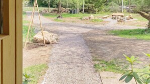 Uma trilha de cascalho leva a uma área rural com árvores e uma pilha de toras.