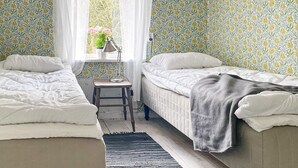 Quarto com duas camas, janela com vista para o verde, escrivaninha com abajur e parede com padrão.
