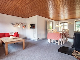 Um quarto acolhedor com teto de madeira, um sofá vermelho, uma mesa de jantar com cadeiras, uma lareira e uma TV fixada na parede.