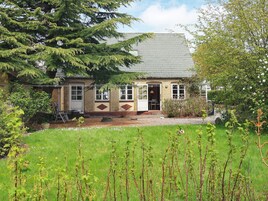 Uma casa de dois andares com fachada de tijolos, varanda frontal e um jardim bem cuidado.