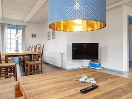 Sala de estar moderna com mesa de jantar de madeira, cadeiras, TV de tela plana e abajur azul perfurado.