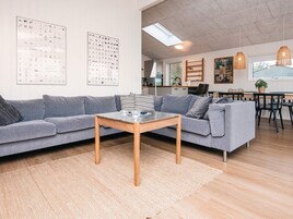 Uma sala de estar moderna com um sofá modular cinza, uma mesa de centro de madeira e uma janela grande com vista.