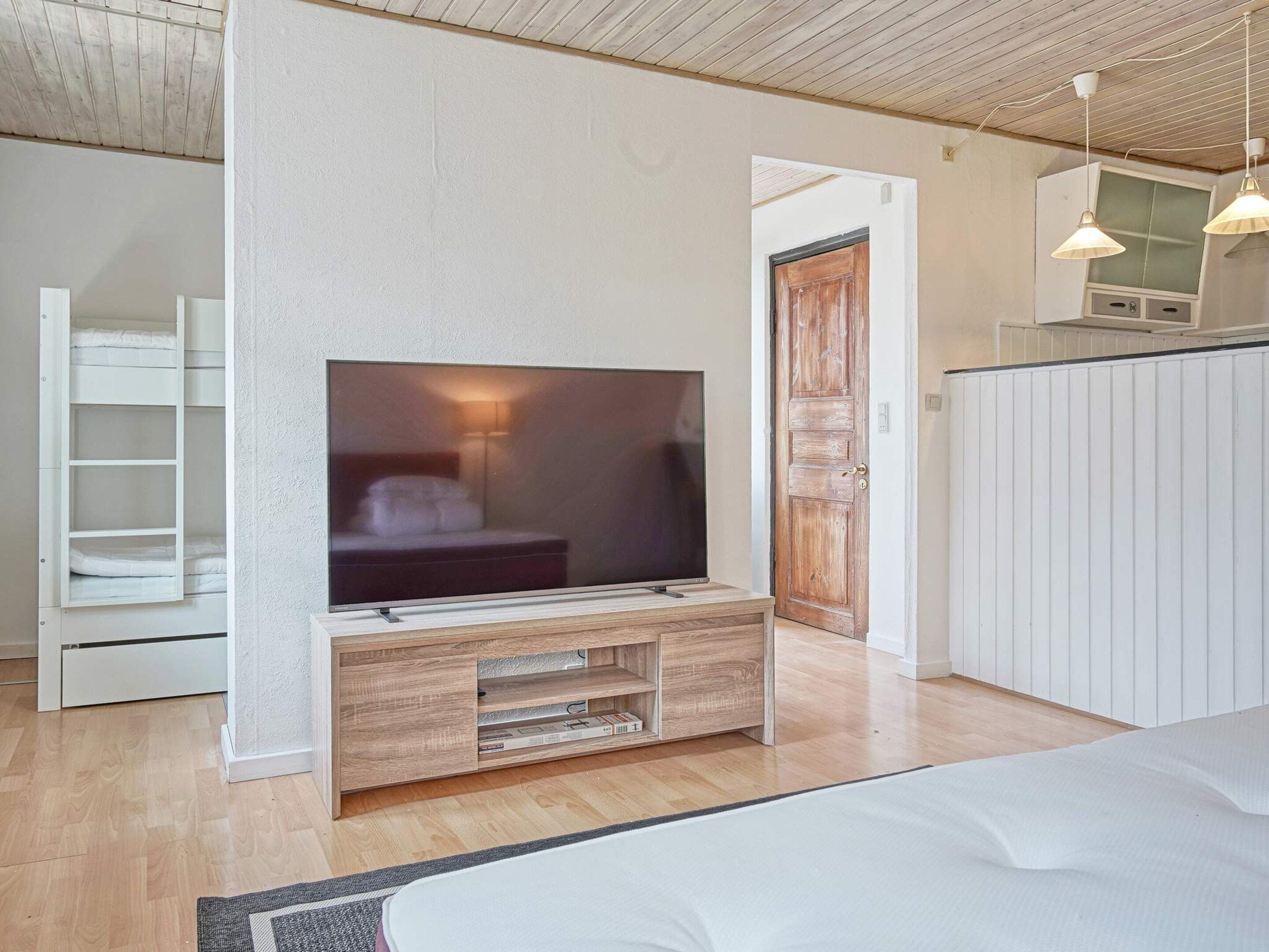 Quarto moderno com televisão de tela plana sobre um suporte de madeira, guarda-roupa e porta que dá para outro cômodo.