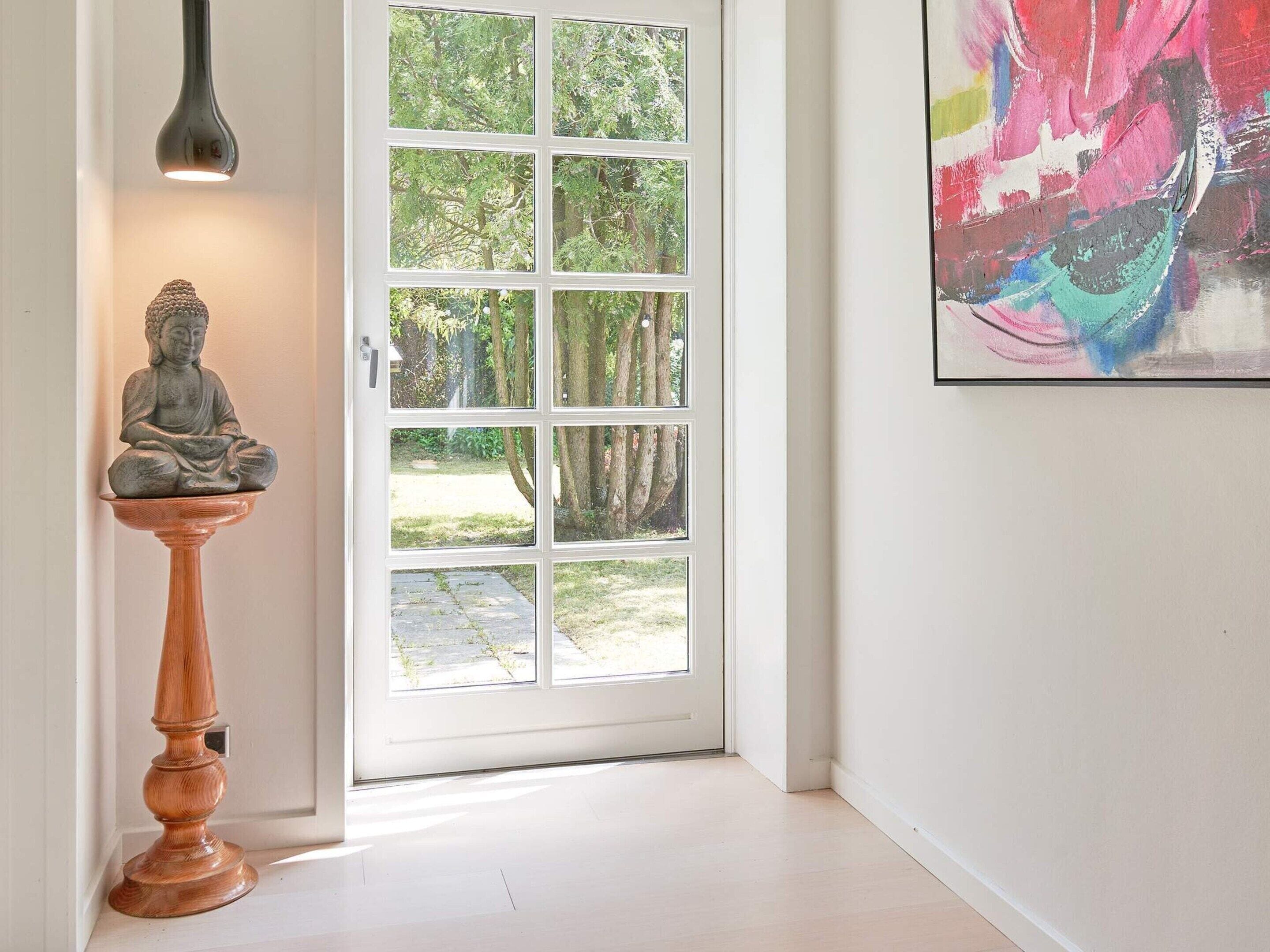 Quarto com uma grande janela, uma estátua de Buda em um pedestal e um quadro abstrato colorido na parede.
