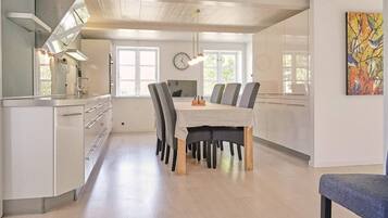 Cozinha moderna com armários brancos, área de jantar com mesa e cadeiras, e uma janela grande que oferece luz natural.