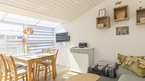 Uma sala de estar moderna com área de jantar, móveis de madeira, televisão de tela plana e objetos decorativos nas prateleiras.