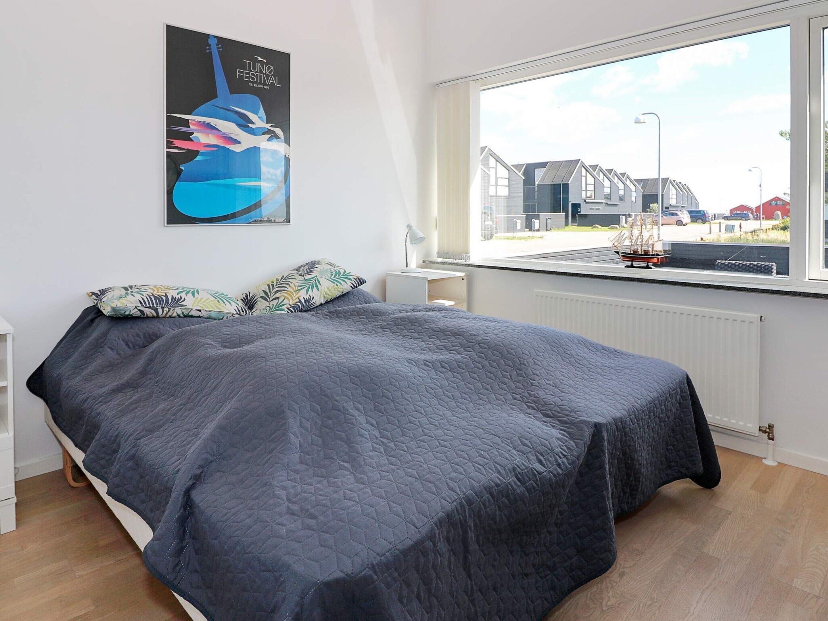 Quarto com cama grande, janela com vista para prédios e um pôster na parede.
