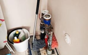 Canto de um quarto com um balde, um esfregão e produtos de limpeza.
