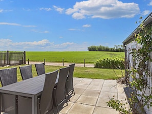 Um pátio externo com mesa e cadeiras, um cercado e vista para um campo verde.