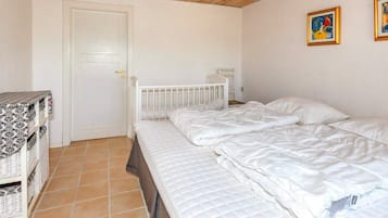 Quarto com cama branca, berço, porta e duas imagens emolduradas na parede.