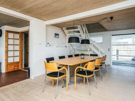Uma sala de jantar ampla com uma mesa de madeira comprida e cadeiras amarelas, uma escadaria e vista para o exterior.