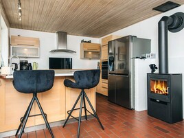 Uma cozinha moderna com uma ilha central, dois banquetes, uma geladeira de aço inoxidável e um fogão a lenha.