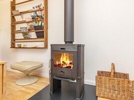 Um quarto com lareira a lenha, uma cesta de vime e uma cadeira.