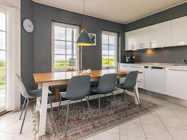 Cozinha moderna com mesa de madeira, quatro cadeiras, tapete e vista para o exterior por grandes janelas.