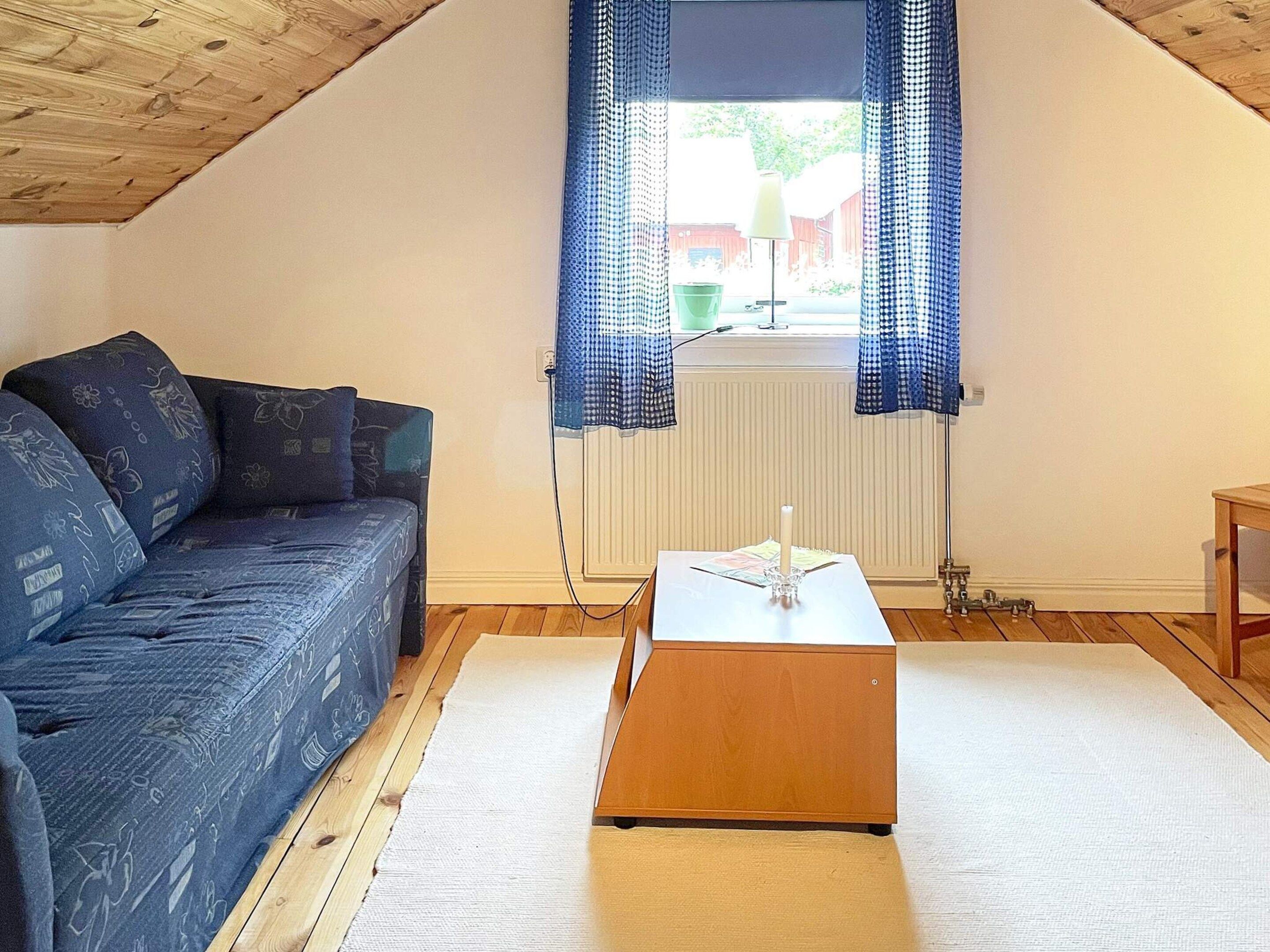 Um quarto aconchegante com teto de madeira, um sofá azul estampado, um tapete branco e uma pequena mesa de madeira.