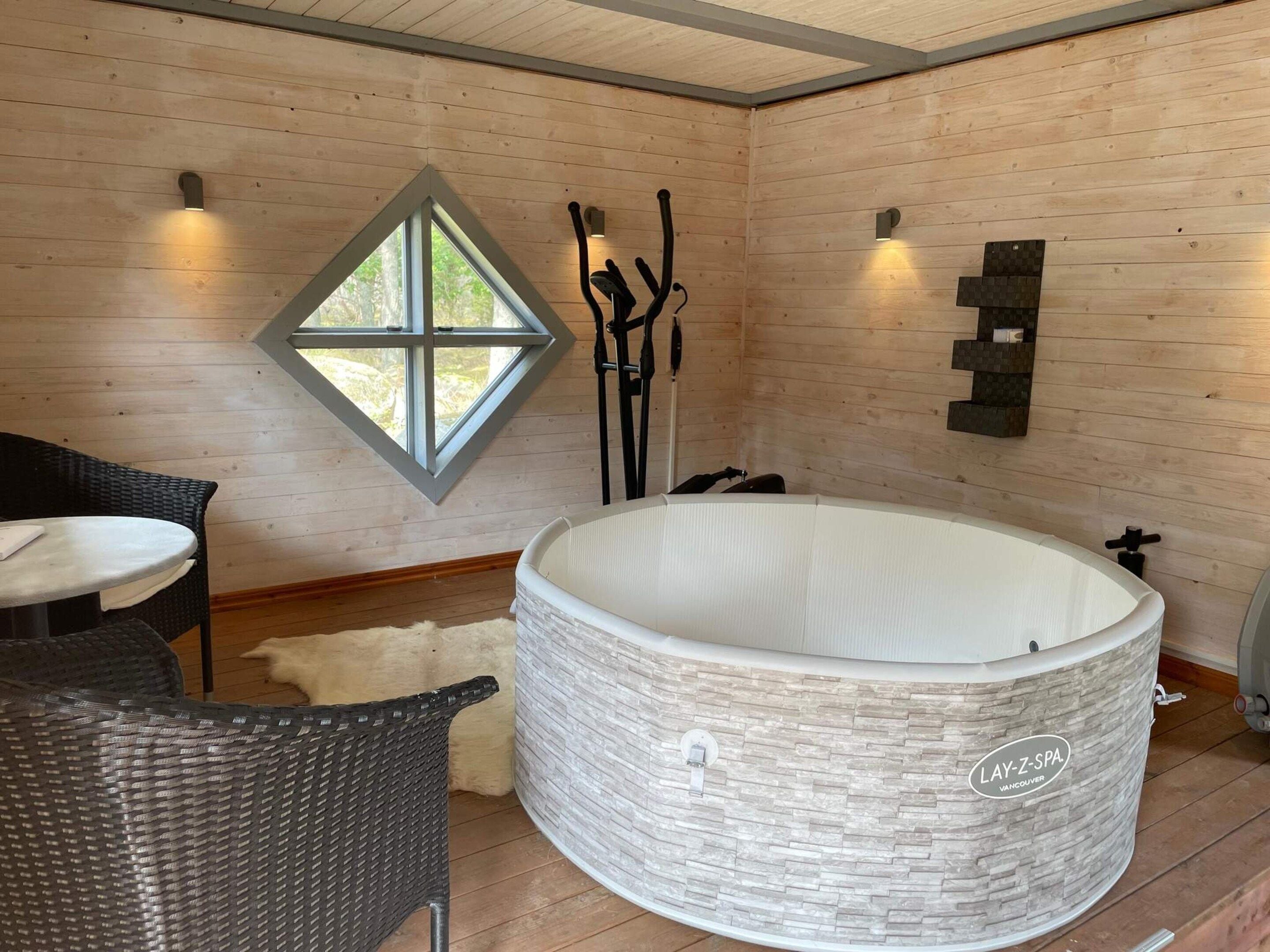 Um quarto de spa com uma banheira de hidromassagem grande e branca, uma janela e um porta-toalhas fixado na parede.
