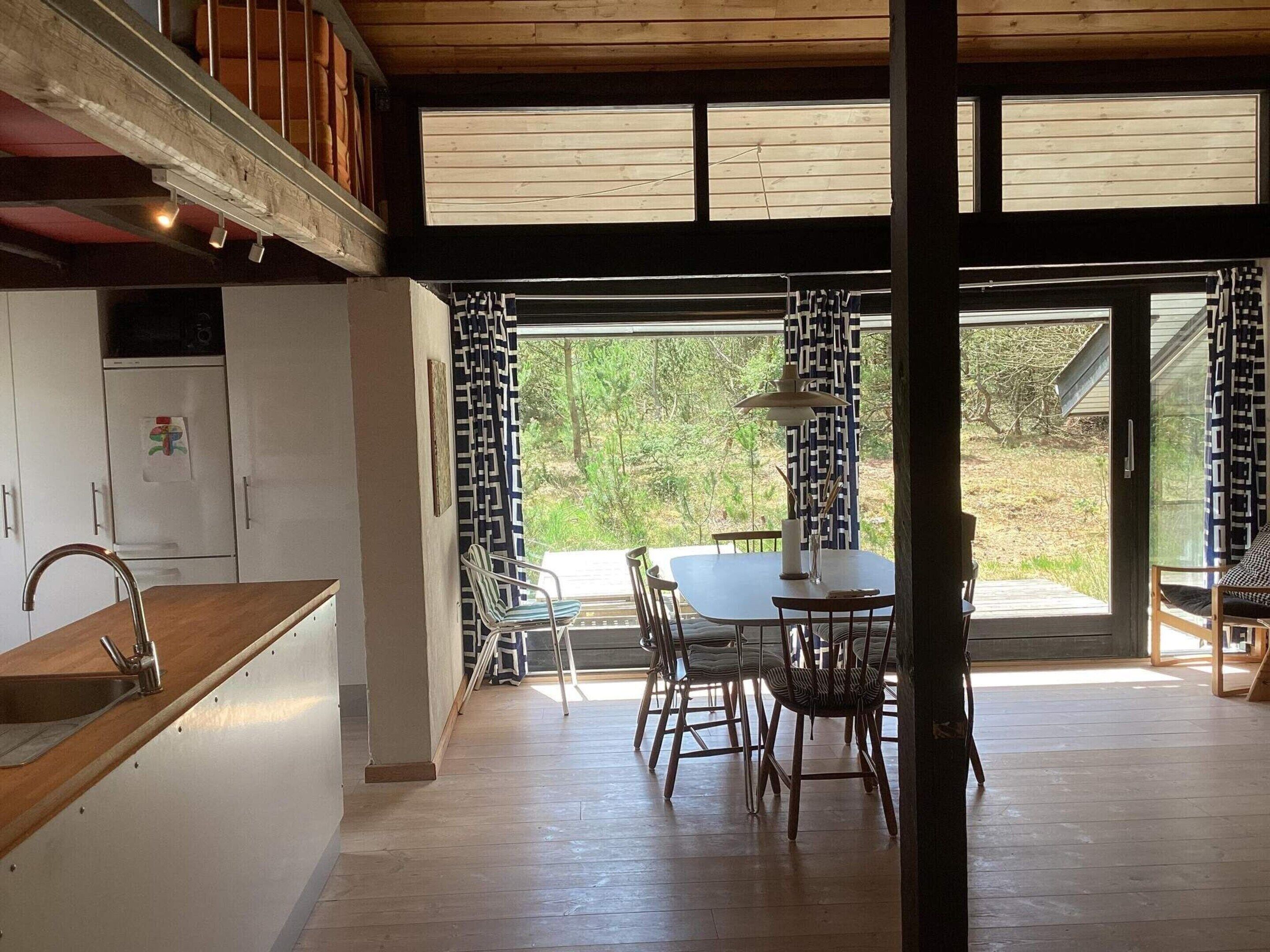 Cozinha moderna com bancada e pia de madeira, espaço de refeições com mesa e cadeiras, e amplas janelas com vista para o exterior.