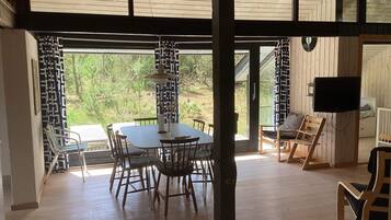 Uma sala de jantar com mesa e cadeiras, uma televisão e vista para o exterior.