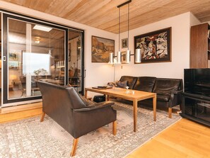 Uma sala de estar moderna com um sofá de couro, uma mesa de centro de madeira e uma televisão.