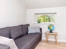 Quarto com sofá cinza, mesa de apoio de madeira com um globo, janela com vista para árvores e parede branca.