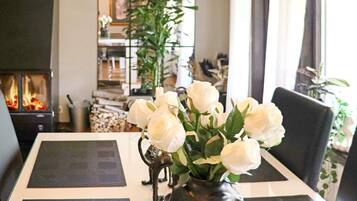 Uma mesa de jantar com um vaso de rosas brancas, um objeto decorativo preto e uma lareira ao fundo.