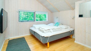 Quarto com cama, duas janelas, televisão e piso de madeira.