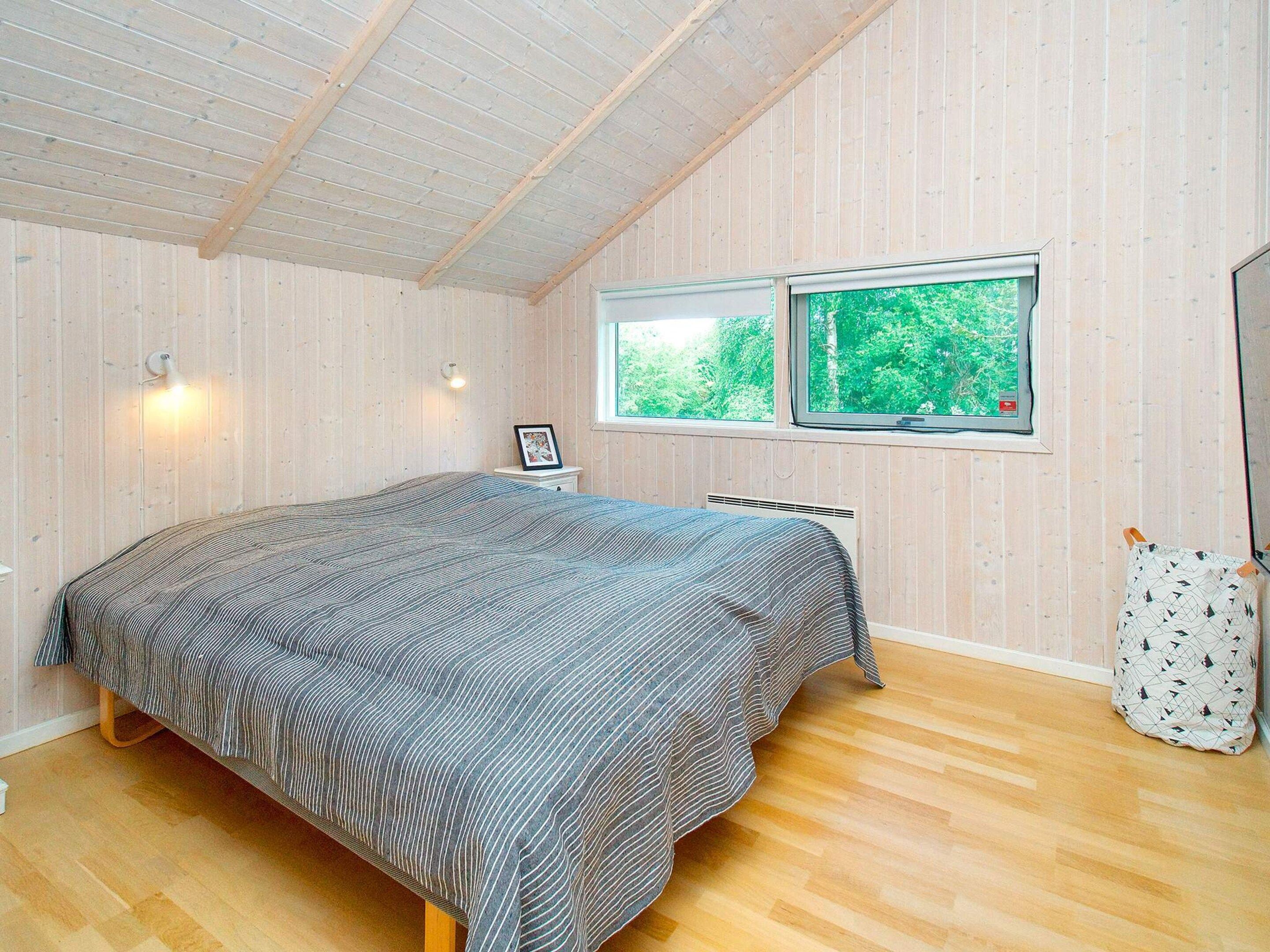 Quarto com cama, duas janelas, mesa de cabeceira e luminária na parede.