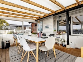 Uma área de refeições ao ar livre coberta, com mesa, cadeiras, um abajur e vista para o exterior.